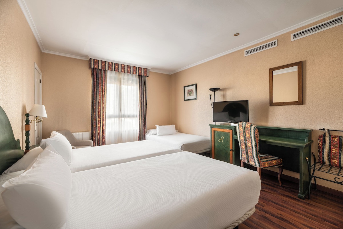 Quarto de hotel com duas camas, uma escrivaninha, uma cadeira, uma televisão e uma janela com cortinas.