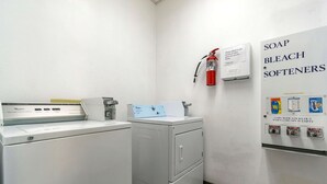 Uma área de lavanderia com máquina de lavar, secadora e um dosador na parede para sabão, alvejante e amaciante.