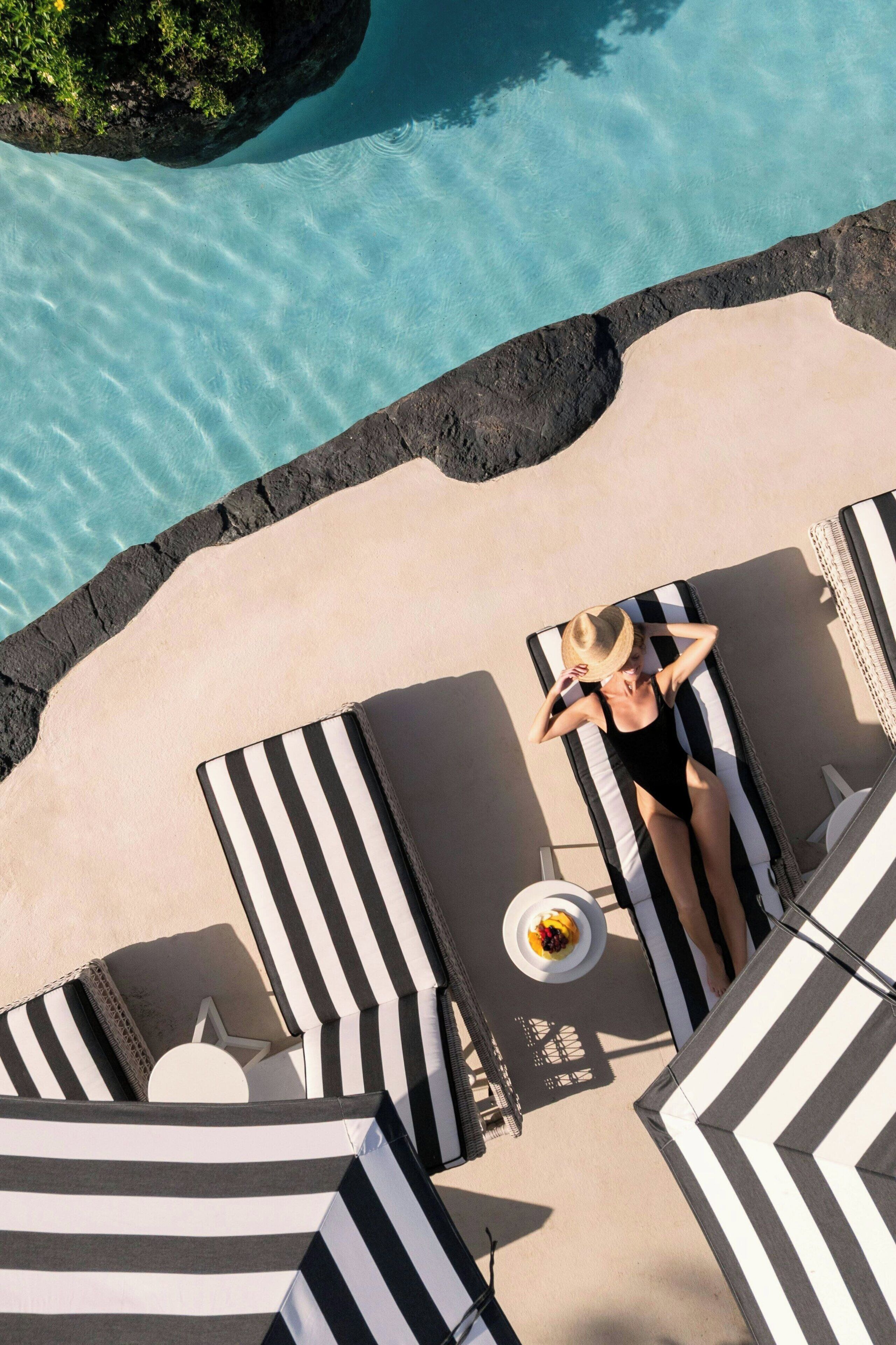 Área de piscina com espreguiçadeiras listradas e uma pessoa relaxando.