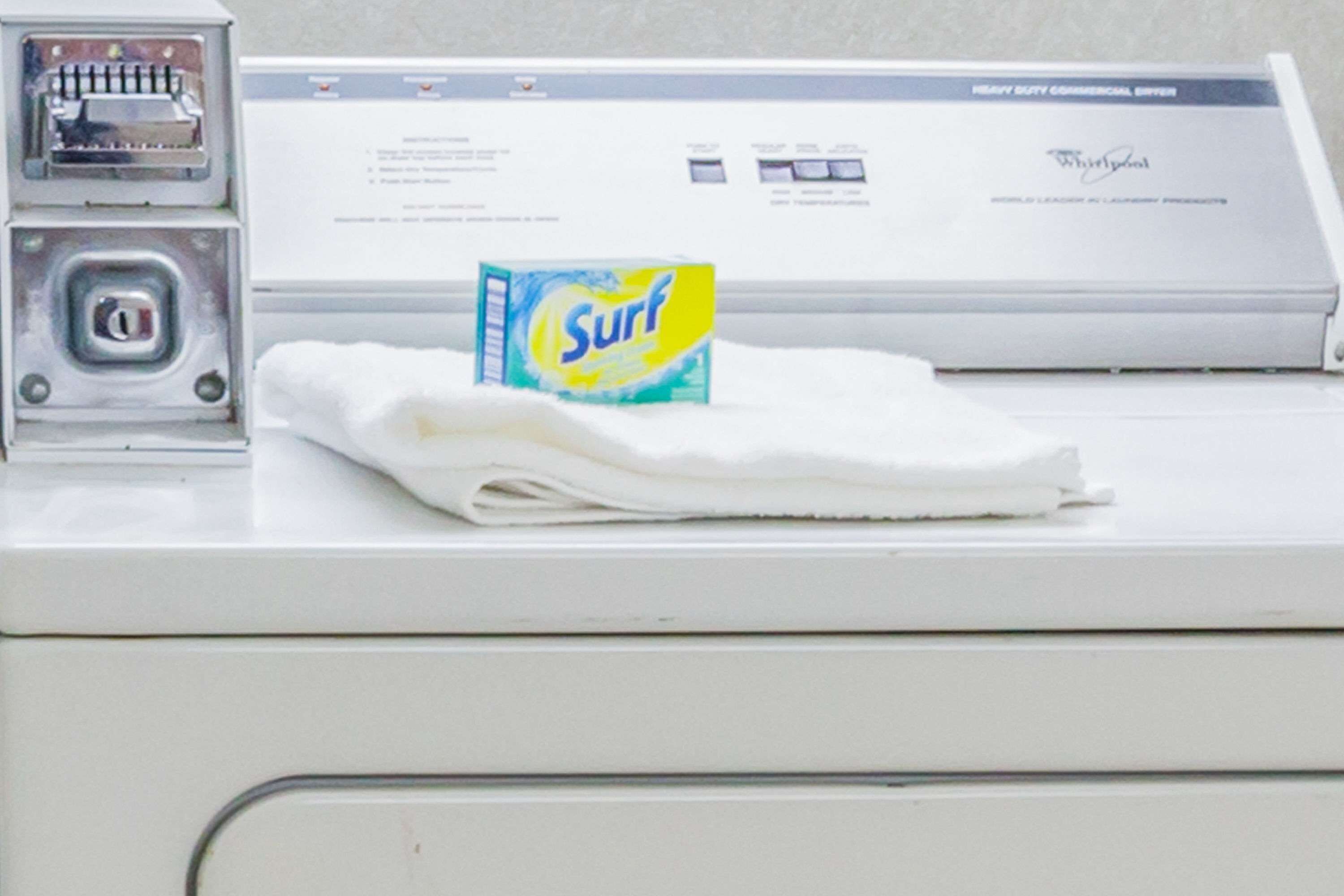 Um eletrodoméstico branco com painel de controle e uma caixa de detergente Surf por cima.