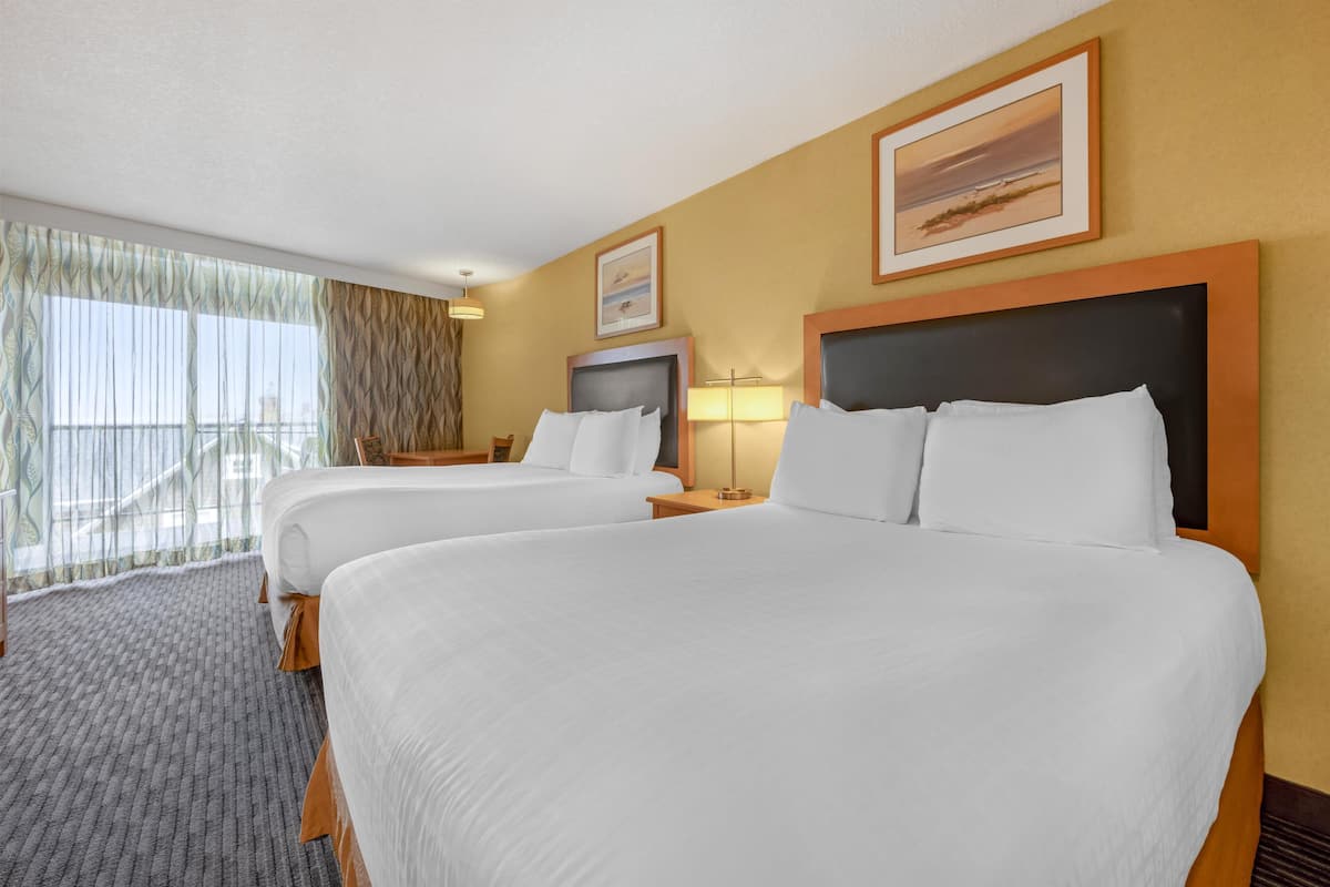 Quarto de hotel com duas camas, televisão, secretária e janela com cortinas.