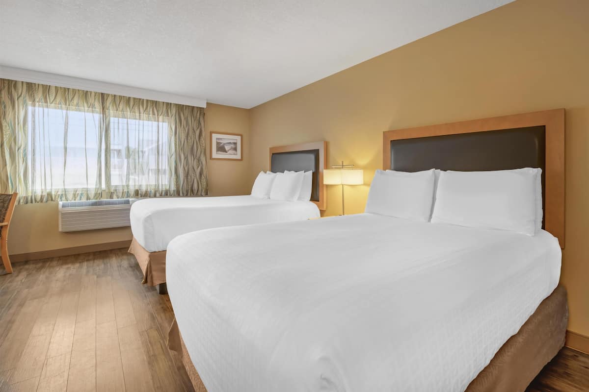 Quarto de hotel com duas camas, janela com cortinas, luminária e um quadro na parede.