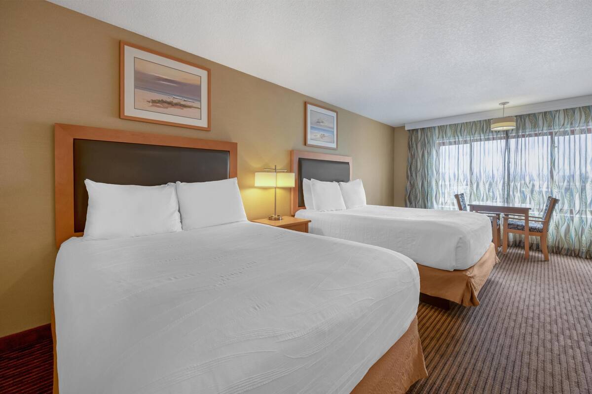 Quarto de hotel com duas camas, uma escrivaninha e uma cadeira.
