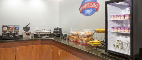 Um balcão de café da manhã com a placa Baymont, cafeteiras, torradeiras e uma geladeira com alimentos.