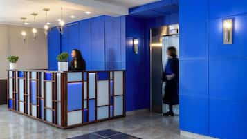Balcão de recepção com parede azul e design moderno, um vaso de planta e um visor digital.