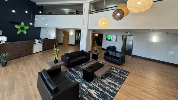 Um hall amplo com balcão de recepção, sofás pretos, mesa de centro e luminárias pendentes.