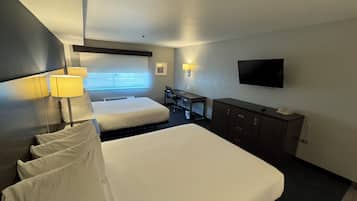 Quarto de hotel com uma cama grande, escrivaninha, cadeira, televisão e janela com vista.
