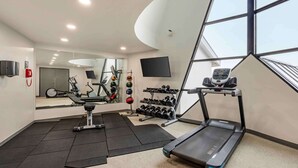 Academia moderna com esteira, banco de musculação e diversos equipamentos de exercício.