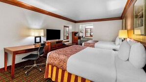 Quarto de hotel com duas camas, uma escrivaninha, uma cadeira, uma televisão e um espelho.