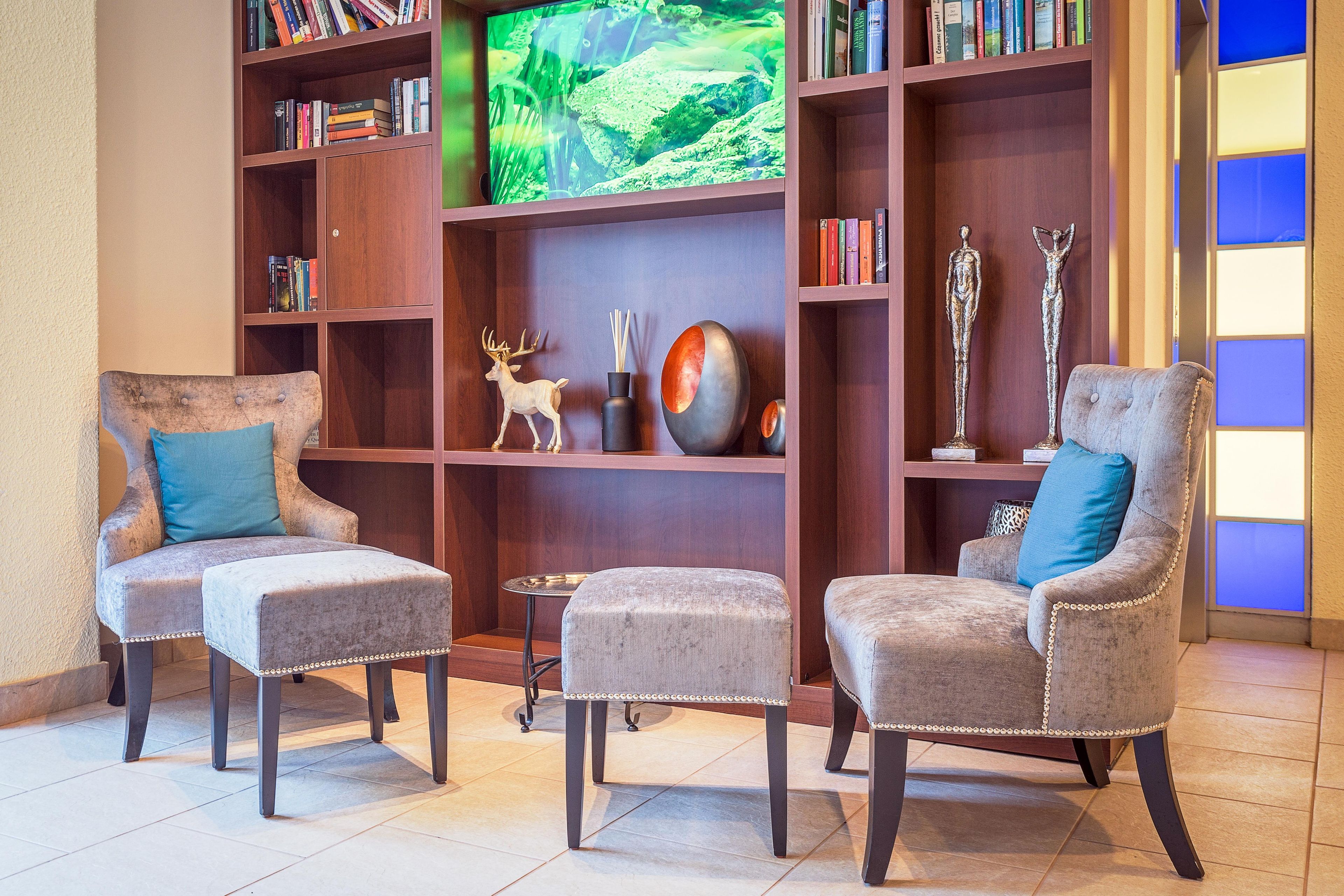 Uma sala de estar moderna com dois poltronas, uma mesa de centro, estante de livros, objetos decorativos e uma televisão.