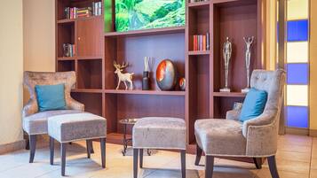 Uma sala de estar moderna com dois poltronas, uma mesa de centro, estante de livros, objetos decorativos e uma televisão.