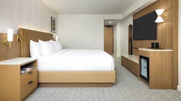 Quarto de hotel com cama, mesas de cabeceira, televisão e minibar.