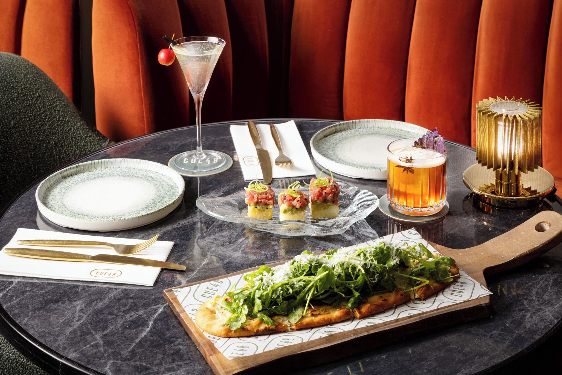 Uma mesa de jantar com pratos, talheres, um copo de martini, um copo de cerveja e uma pizza.