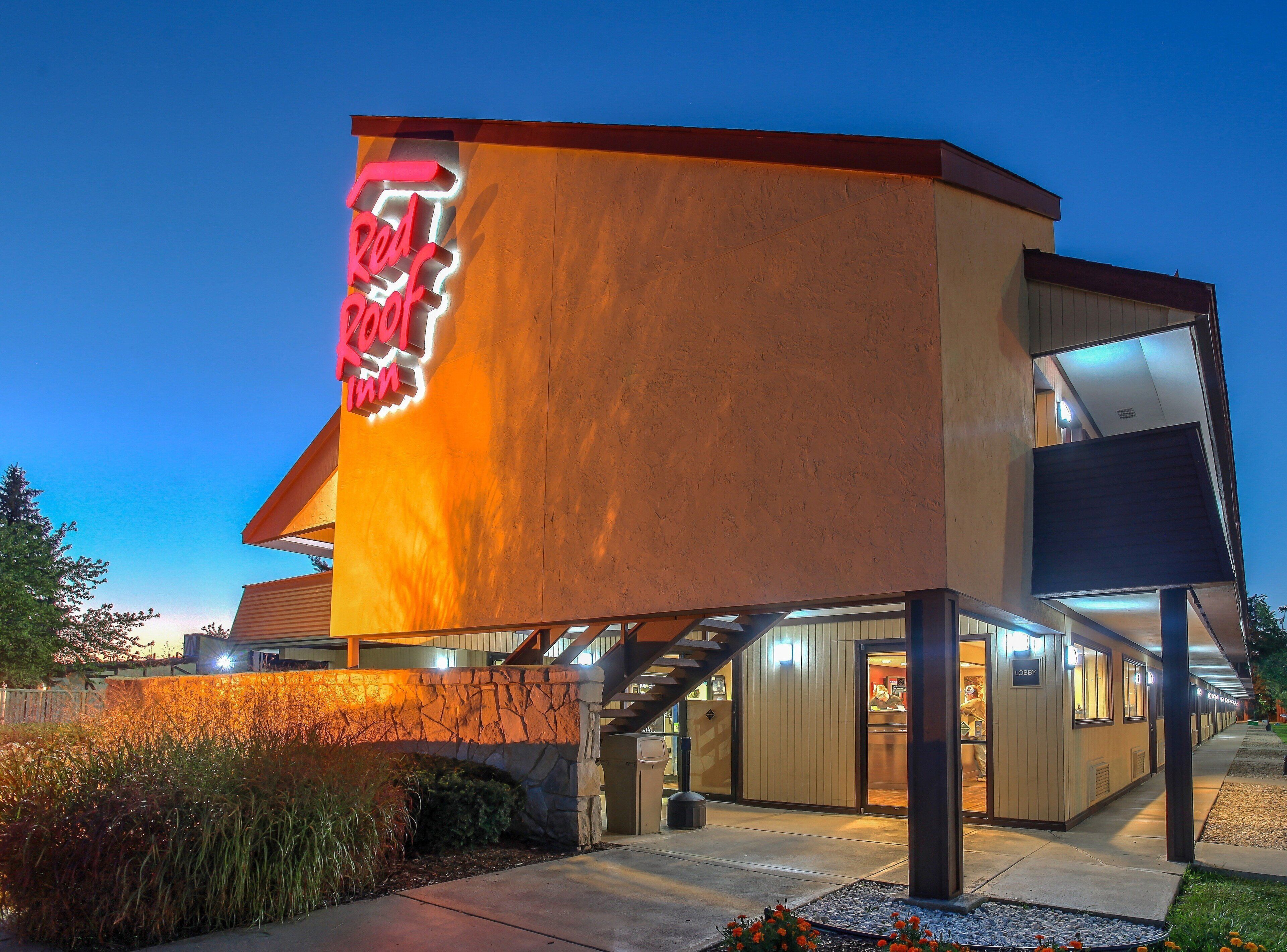 Um Red Roof Inn com design moderno, com um letreiro de neon destacado, área de lobby e escada que leva à entrada.