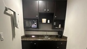 Cozinha compacta com armários escuros, micro-ondas e pia.