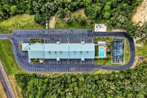 Vista aérea de um edifício com estacionamento, piscina e quadra de tênis.