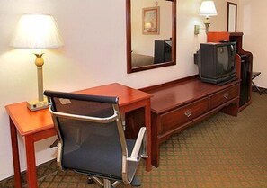 Quarto de hotel com secretária de madeira, uma cadeira, televisão e espelho.