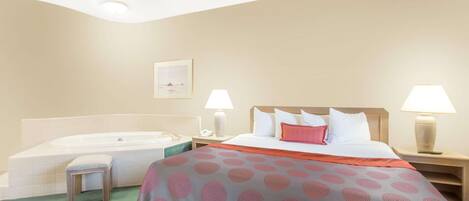 Quarto de hotel com cama, duas luminárias de cabeceira, mesa de cabeceira, um banquinho e uma banheira.