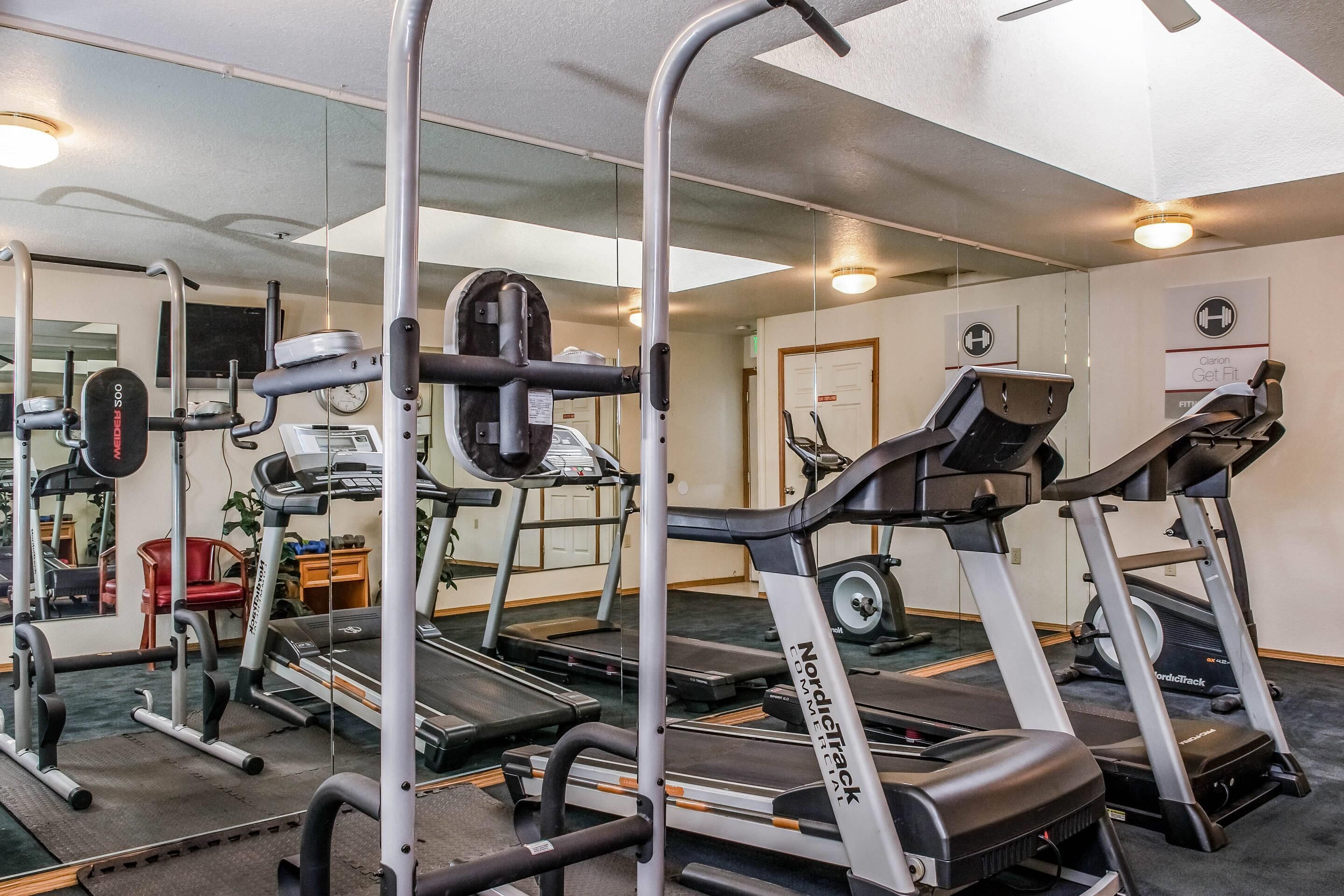 Uma academia com esteiras, máquinas de musculação e um espelho refletindo os equipamentos.