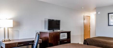 Quarto de hotel com uma mesa, televisão, micro-ondas, duas camas e uma porta.