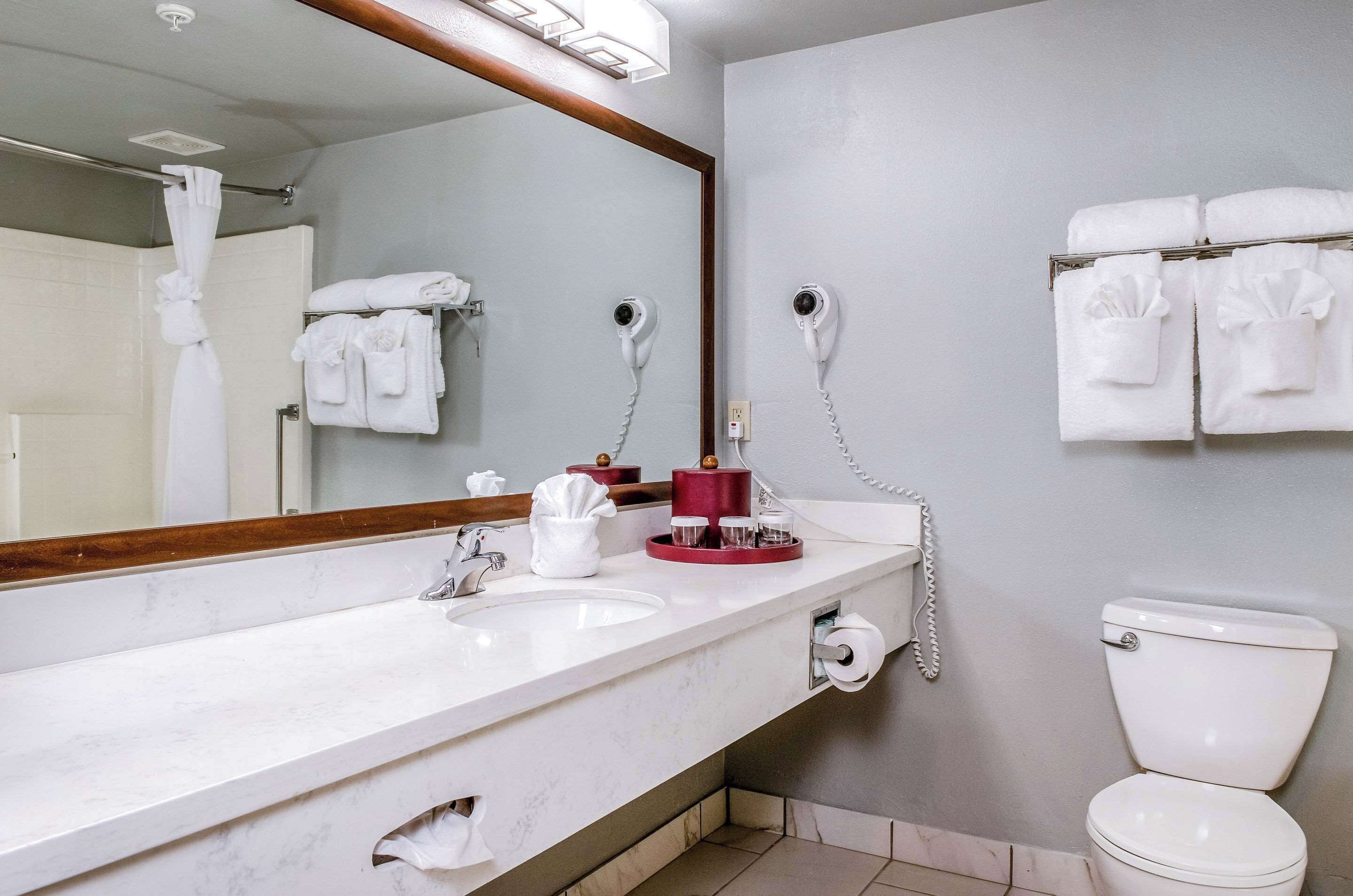 Uma casa de banho com uma pia branca, um espelho, uma sanita e um secador de cabelo fixado na parede.