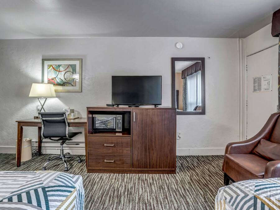 Quarto de hotel com uma cama, uma escrivaninha com cadeira, uma televisão e uma poltrona de couro.