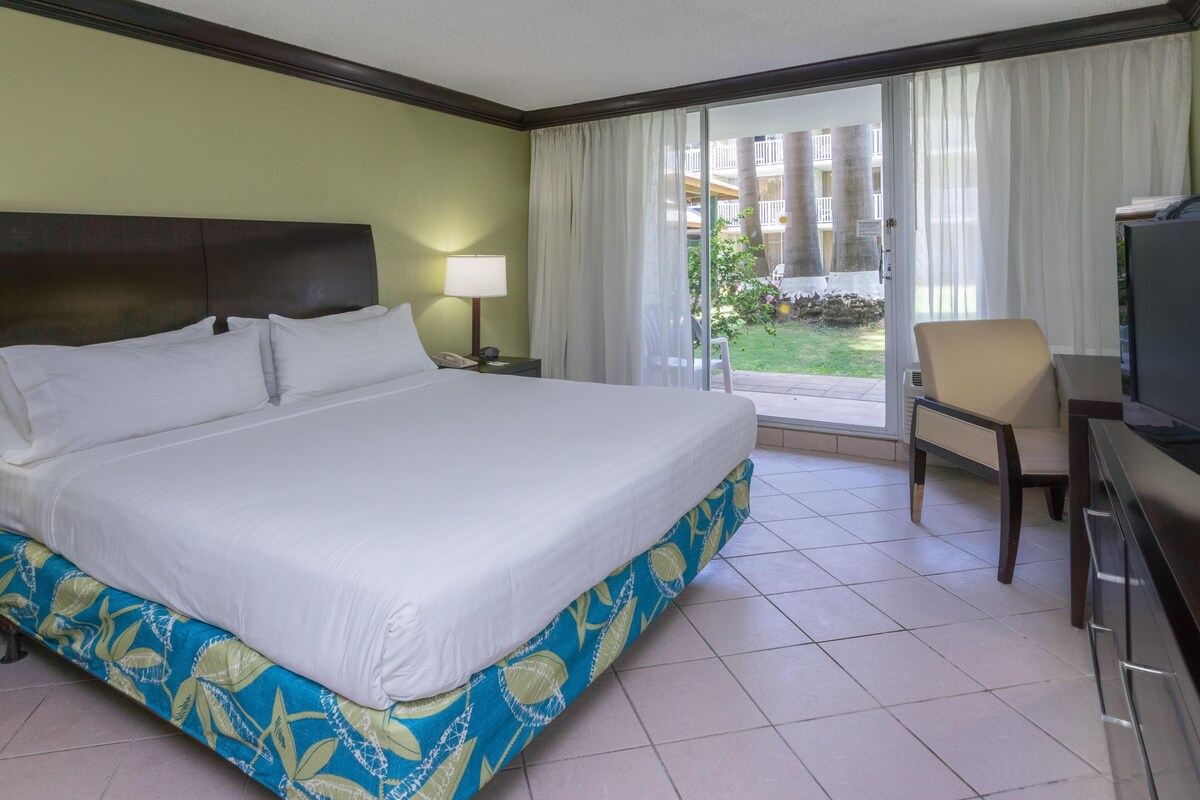 Quarto de hotel com uma cama grande, uma mesa com cadeira, uma televisão e vista para a varanda.
