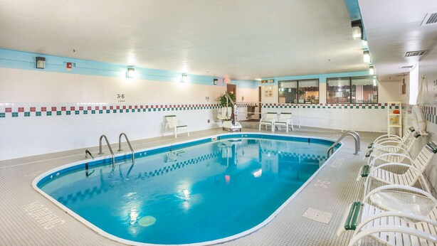 Piscina interior com faixas demarcadas, chão em azulejo e cadeiras de descanso brancas na borda.