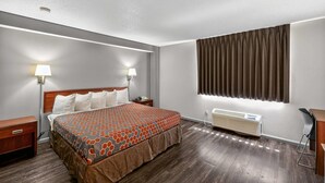 Quarto de hotel com uma cama grande, duas luminárias de cabeceira, uma janela com cortinas, um aquecedor e uma escrivaninha com uma cadeira.