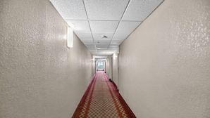 Um corredor comprido e estreito, com paredes brancas e um tapete estampado.