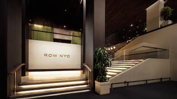 Interior moderno com uma escadaria, uma placa com a inscrição 'ROW NYC' e uma planta em vaso.