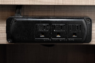 Tome de eletricidade preto com três tomadas e um interruptor, fixado numa superfície de madeira.