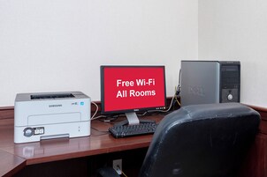 Uma escrivaninha com uma impressora, um monitor e um computador de mesa.