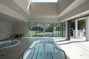 Piscina interior moderna com paredes de vidro, oferecendo vista clara para o exterior, e chão revestido de azulejos.