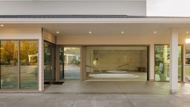 Um edifício moderno com entrada de vidro, piscina interior visível e escadaria que leva a um andar superior.