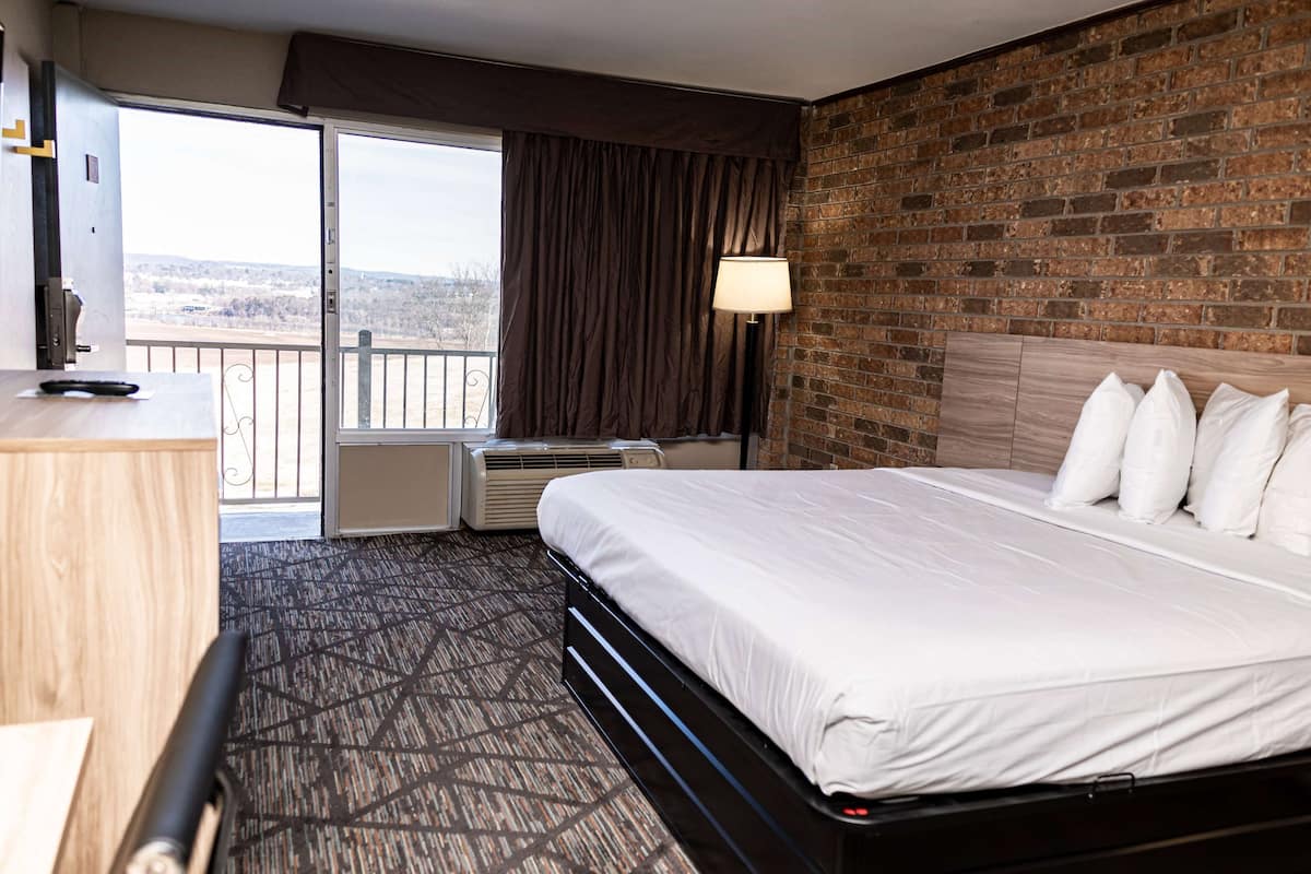 Quarto de hotel com uma cama grande, uma mesa, uma cadeira, uma janela com cortinas, um aparelho de ar condicionado e uma parede de tijolos.