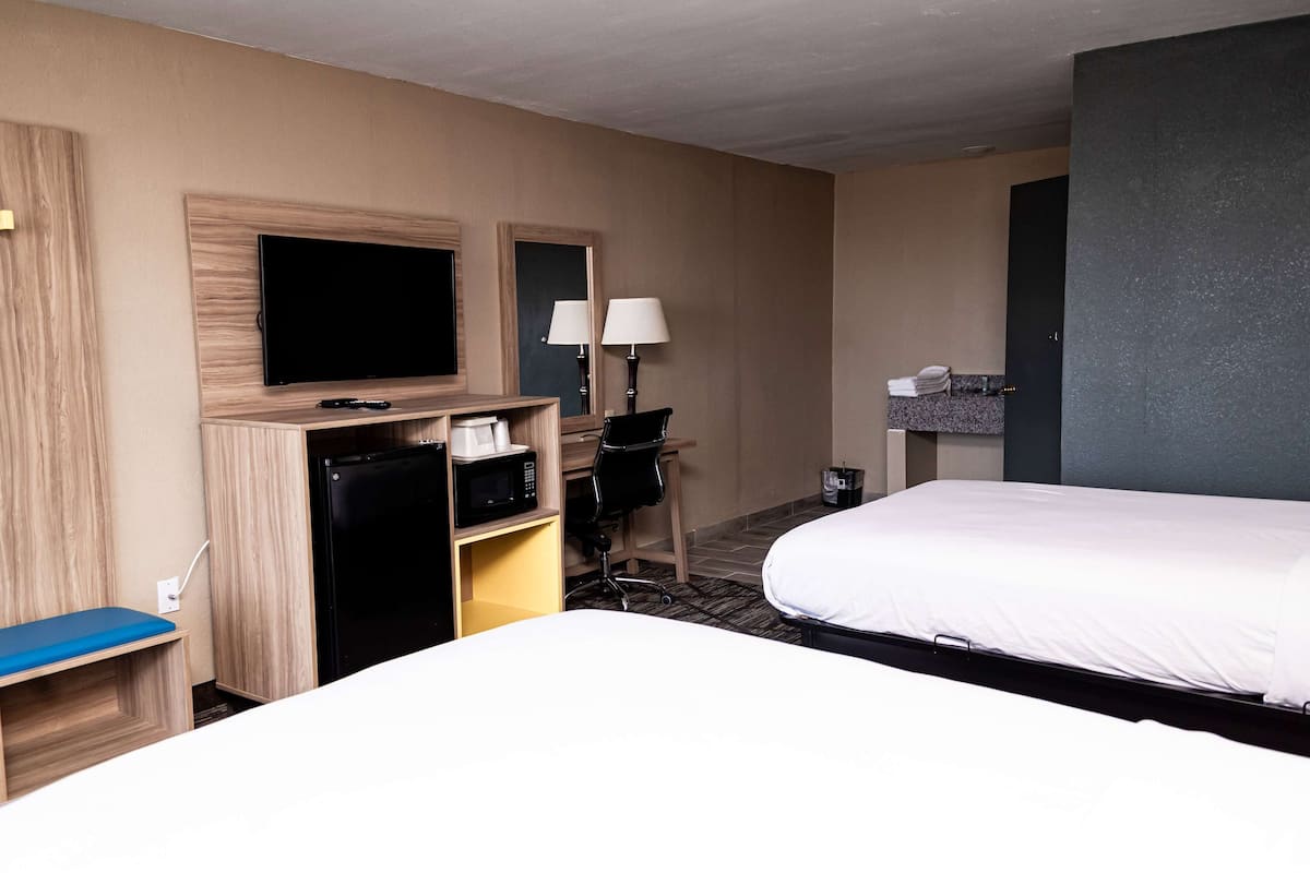 Quarto de hotel com cama, escrivaninha com computador, televisão, micro-ondas e uma pequena área de estar.