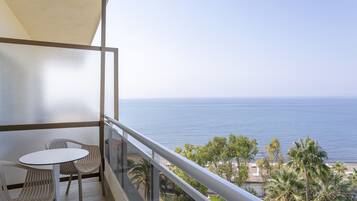 Uma varanda com vista para o mar, duas cadeiras de vime e uma mesa pequena.