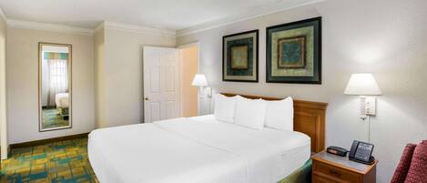 Quarto de hotel com uma cama grande, uma mesa de cabeceira com telefone, uma cadeira e duas fotos emolduradas na parede.