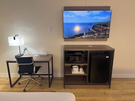 Quarto de hotel com escrivaninha, cadeira, luminária, TV de tela plana e minibar.
