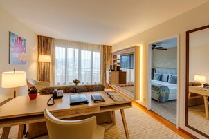 Quarto de hotel com escrivaninha, cadeira, cama, televisão e vista para a cidade.