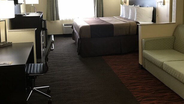 Quarto de hotel com cama, escrivaninha, cadeira, sofá e televisão.