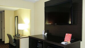 Quarto de hotel com televisão de tela plana fixada na parede, uma escrivaninha com luminária e uma cadeira.