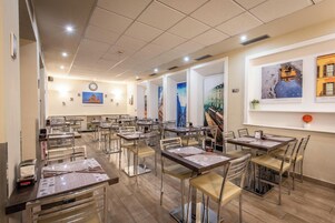 Um restaurante com várias mesas e cadeiras, um relógio na parede e obras de arte emolduradas nas paredes.