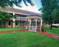 Um edifício com um alpendre coberto, um caminho vermelho e gramados verdes.