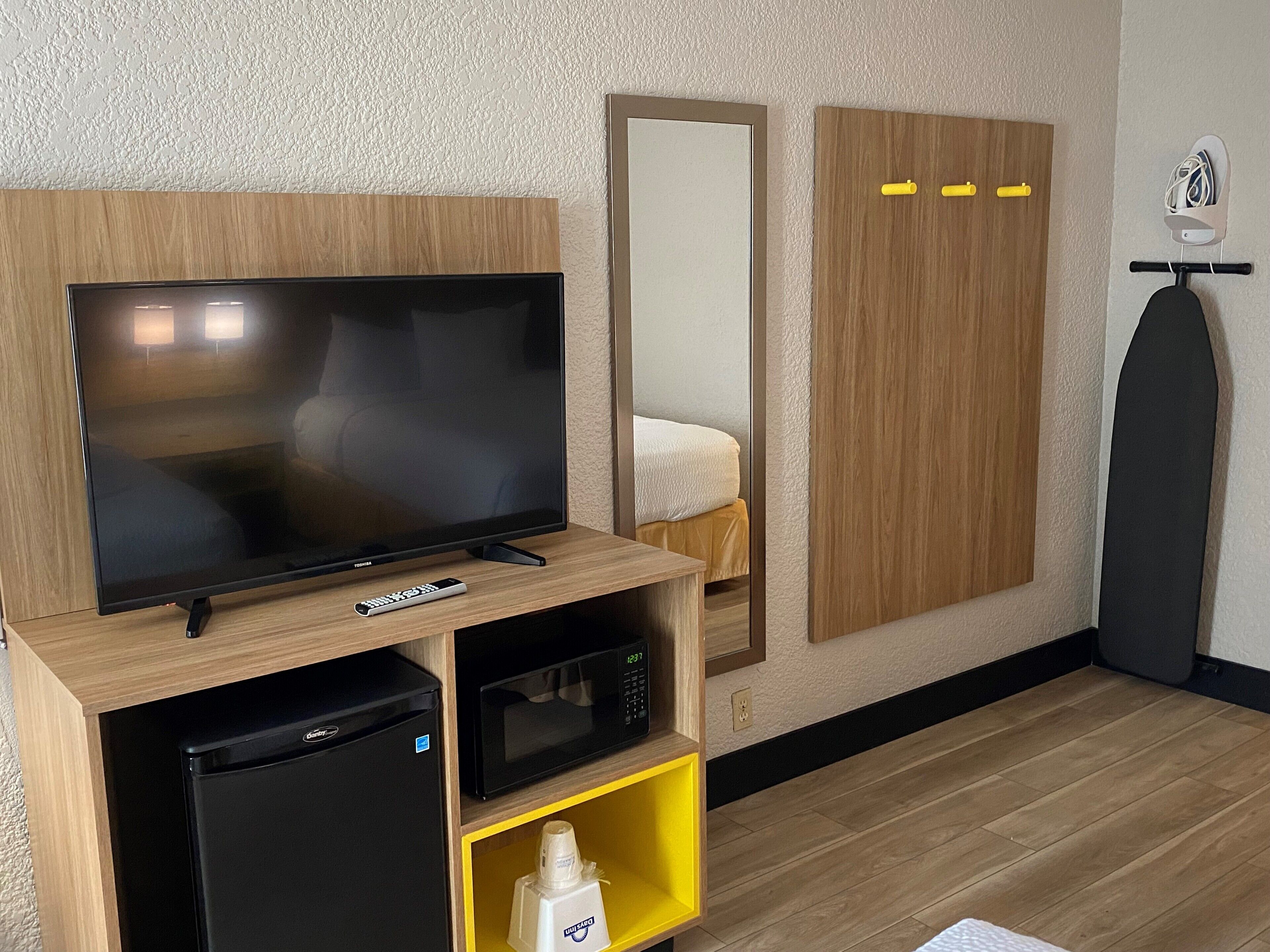 Quarto de hotel com televisão de tela plana, mini-geladeira, micro-ondas e prateleira amarela.
