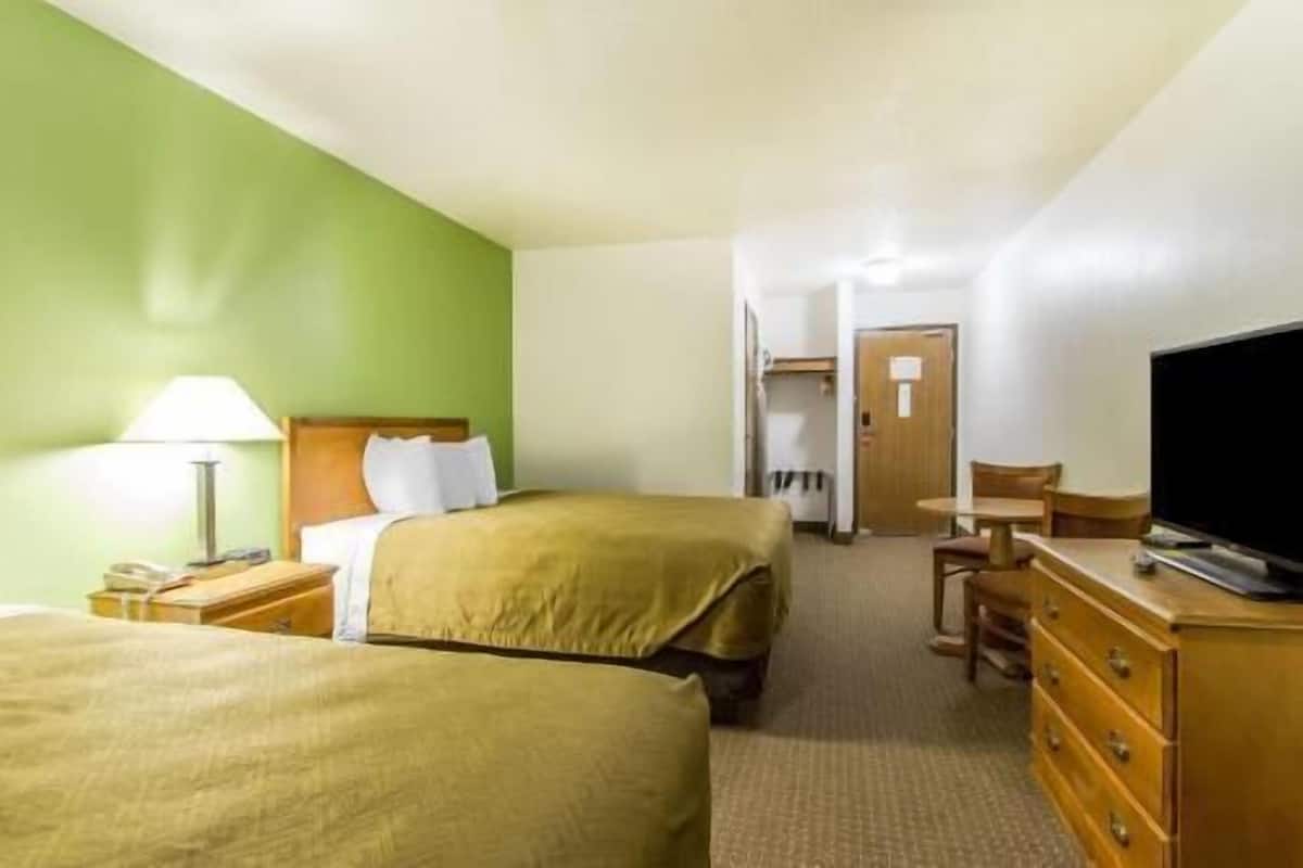 Quarto de hotel com duas camas, televisão, cômoda e escrivaninha com cadeira.