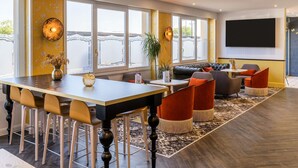 Quarto de hotel moderno com área de refeições, sofá e uma grande tela de TV.