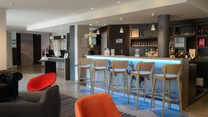 Uma área de bar moderna com balcão, banquetas e um espaço de estar com uma cadeira vermelha.