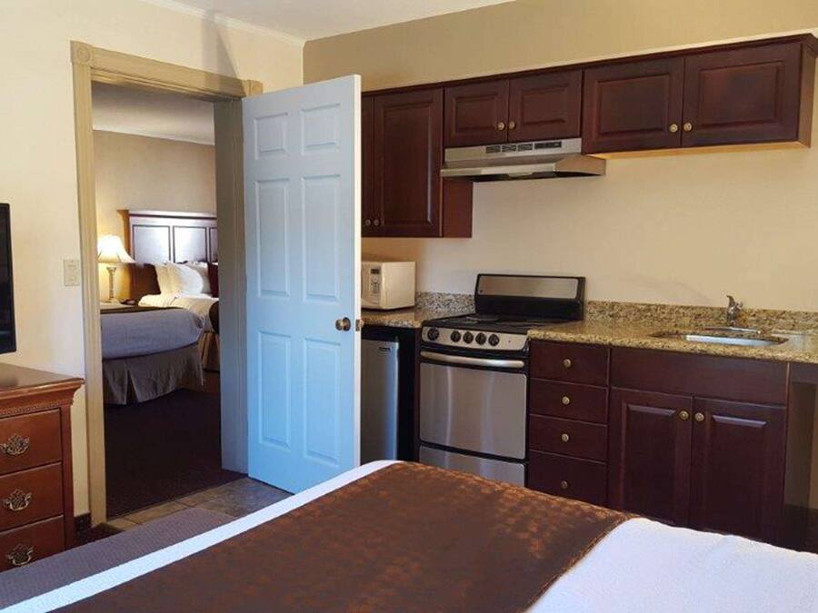 Quarto de hotel pequeno com cama, TV, cozinha compacta com fogão e micro-ondas, e porta para o banheiro.
